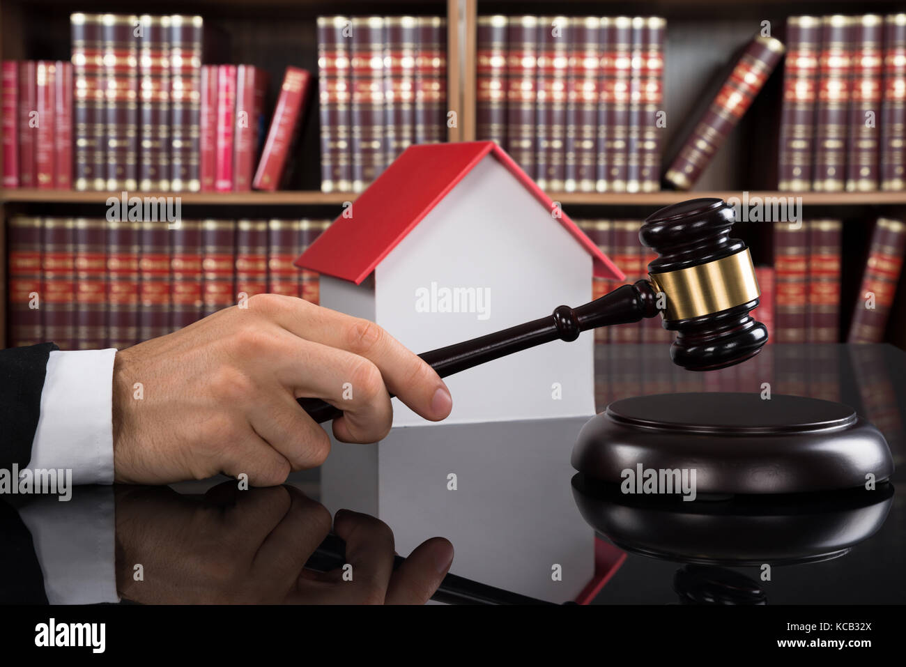 Judge In A Courtroom Striking The Gavel In Front Of House Model On Desk ...