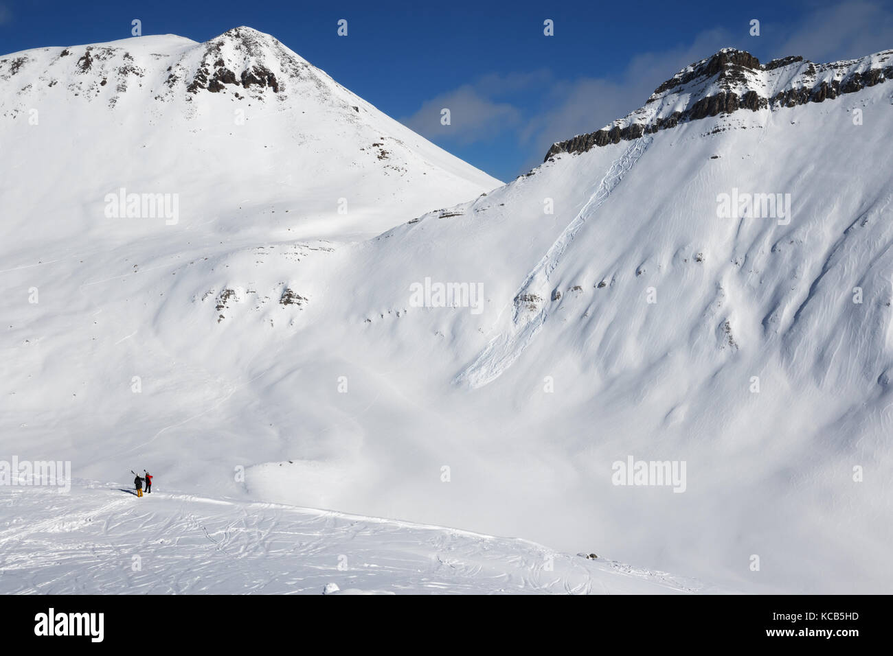 Two skiers with skis on his shoulder and off-piste slope with traces of ...