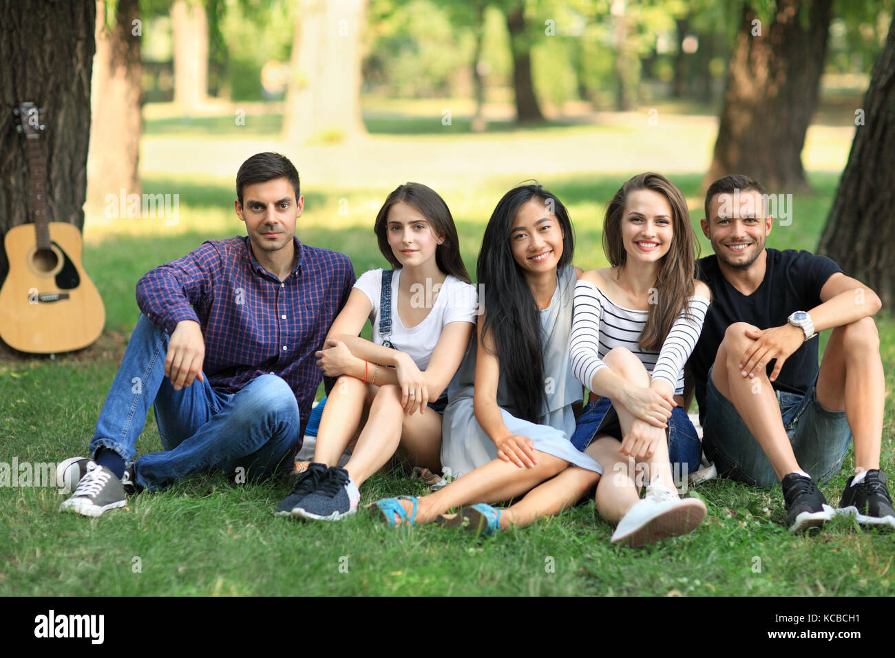 Group of friends sitting in park on grass and looking at camera. Men ...