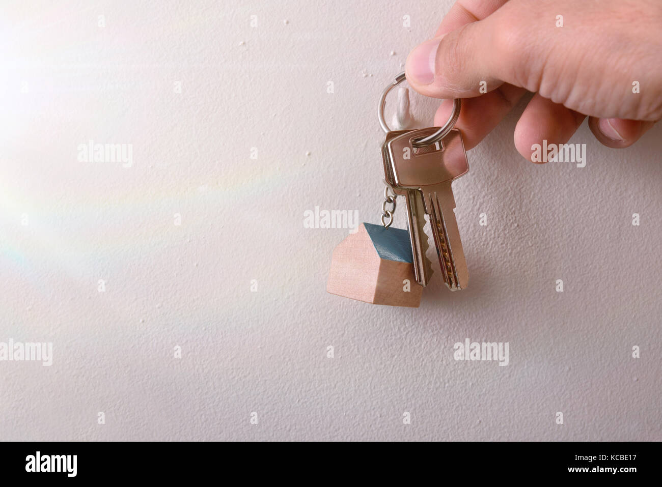 Hands hanging keys with keyring on a hook on the wall of a house with ...
