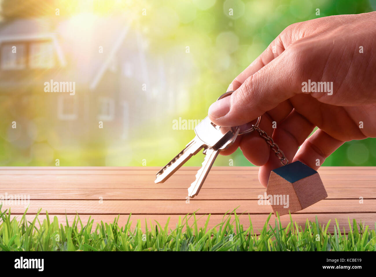 Keys in hand on a wooden table with house image on nature background ...