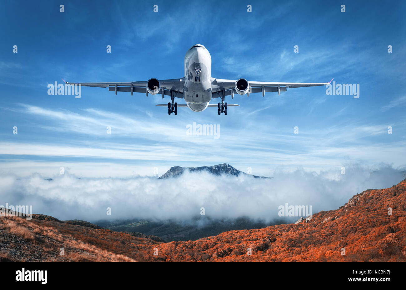 Airplane is flying over low clouds and mountains with autumn forest ...