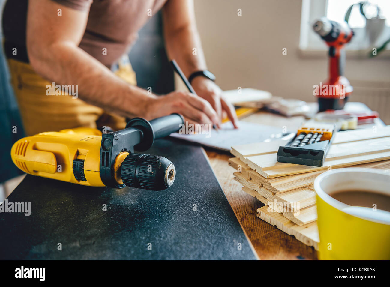 Yellow power drill and man making draft plan using pencil on the table ...