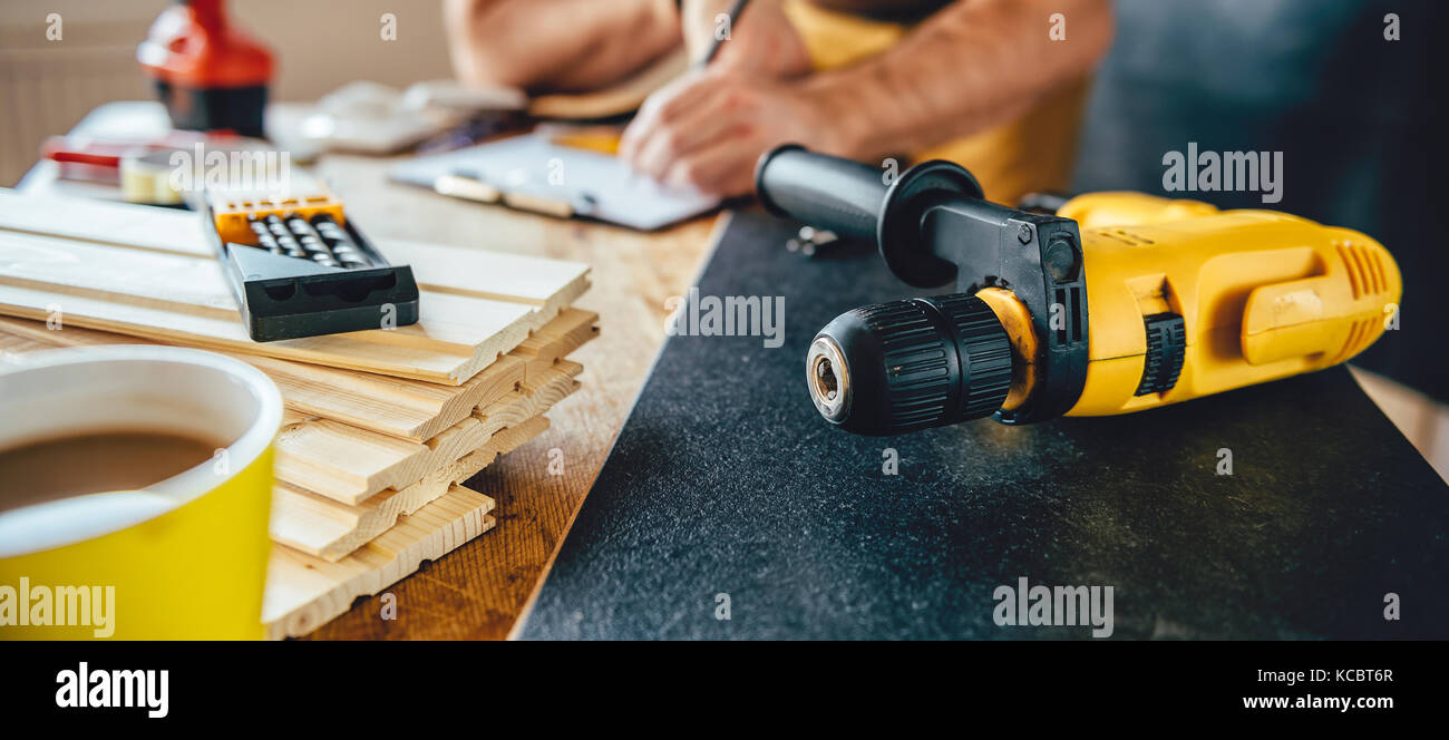 Yellow power drill and man making draft plan using pencil on the table ...