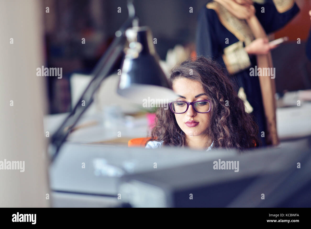 Portrait of smiling pretty young business woman in glasses sitting on ...