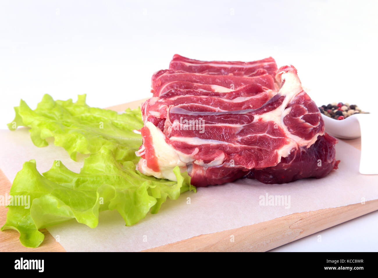 Raw beef edges, lettuce leaf and spices on wooden desk isolated on ...