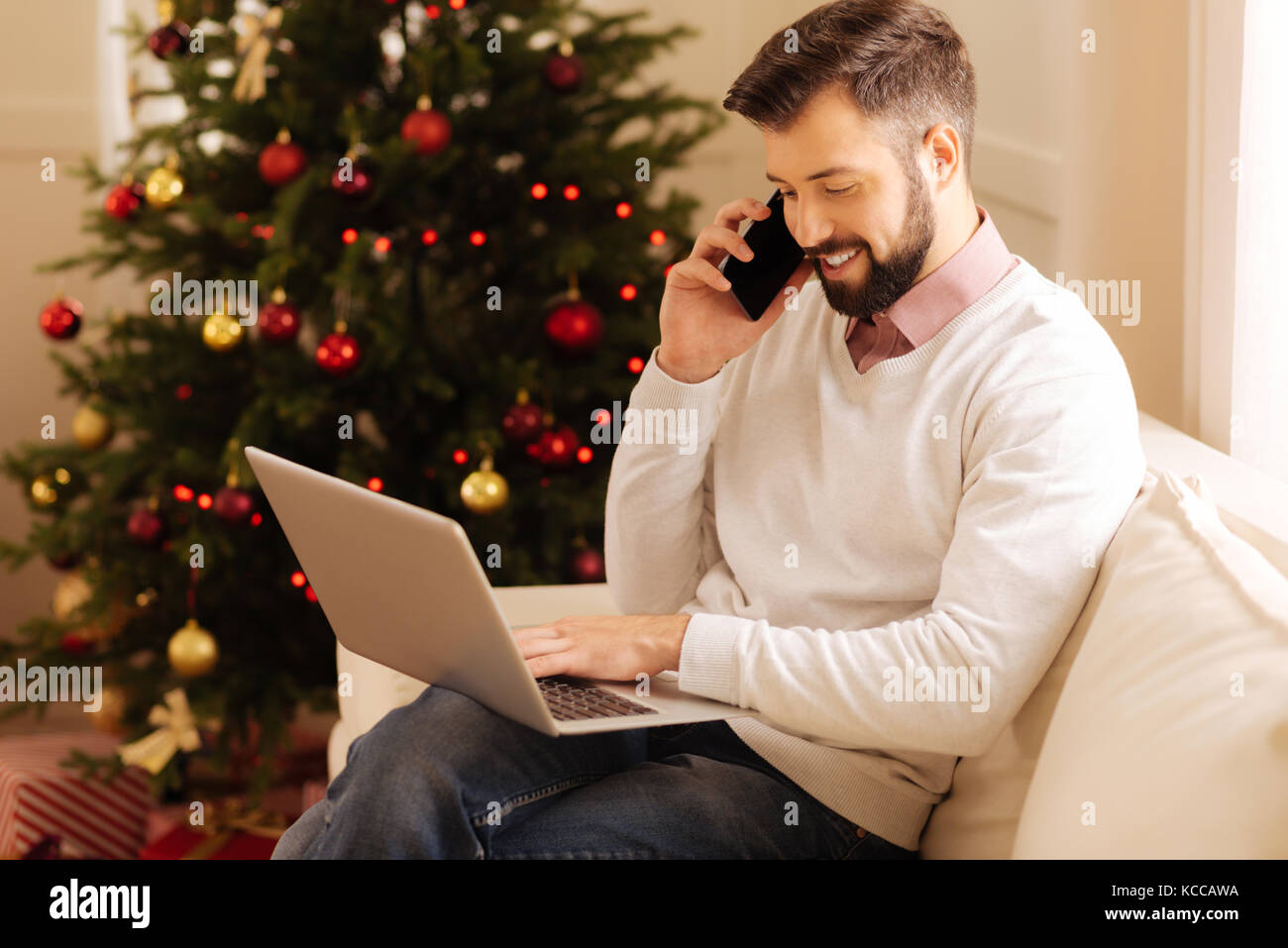 Smiling man talking on phone while typing on laptop Stock Photo - Alamy