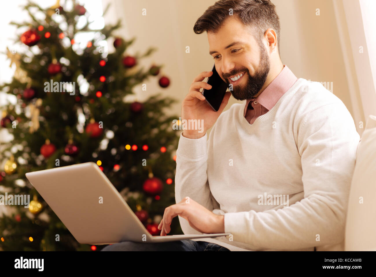 Pleasant man making phone call while using laptop Stock Photo - Alamy