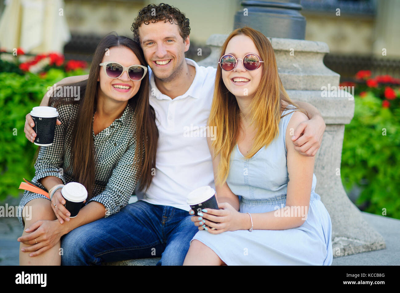 Two girls and a guy are drinking coffee and talking lively. Friends are ...