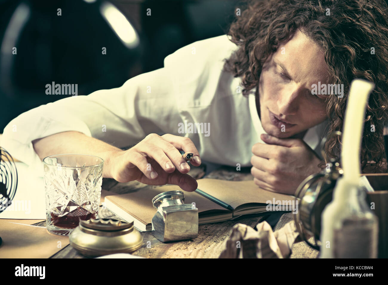 Writer at work. Handsome young writer sitting at the table and writing ...