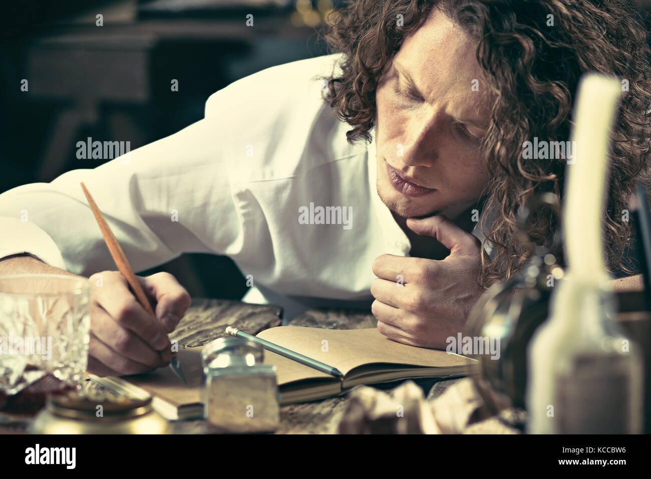 Writer at work. Handsome young writer sitting at the table and writing ...