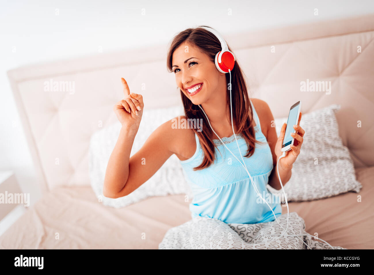 Beautiful smiling girl relaxing in bed. She is having fun and listening ...
