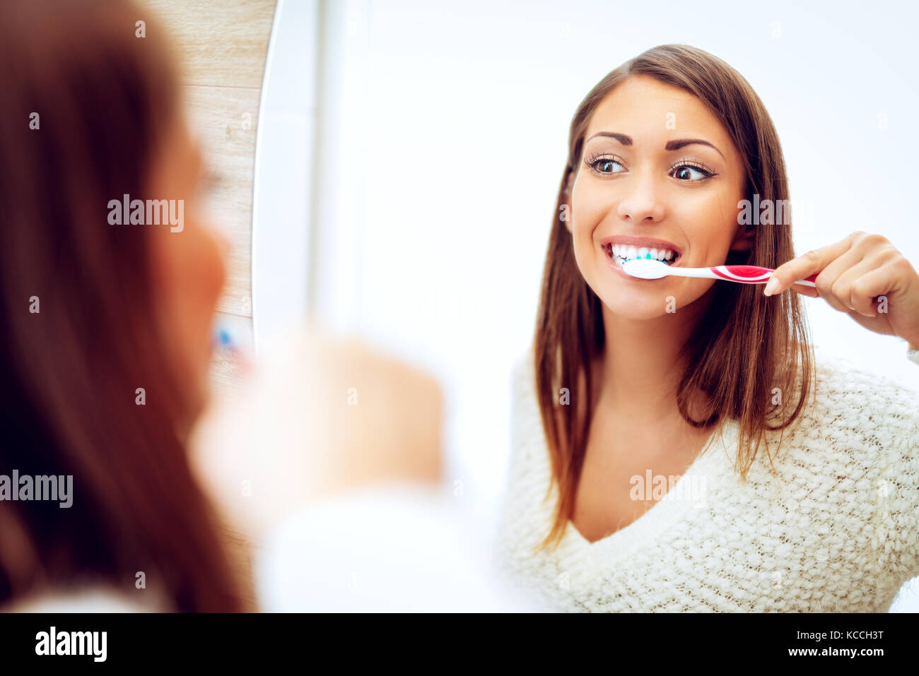 Beautiful Young Woman Brushing Teeth In Front Of Her Bathroom Mirror