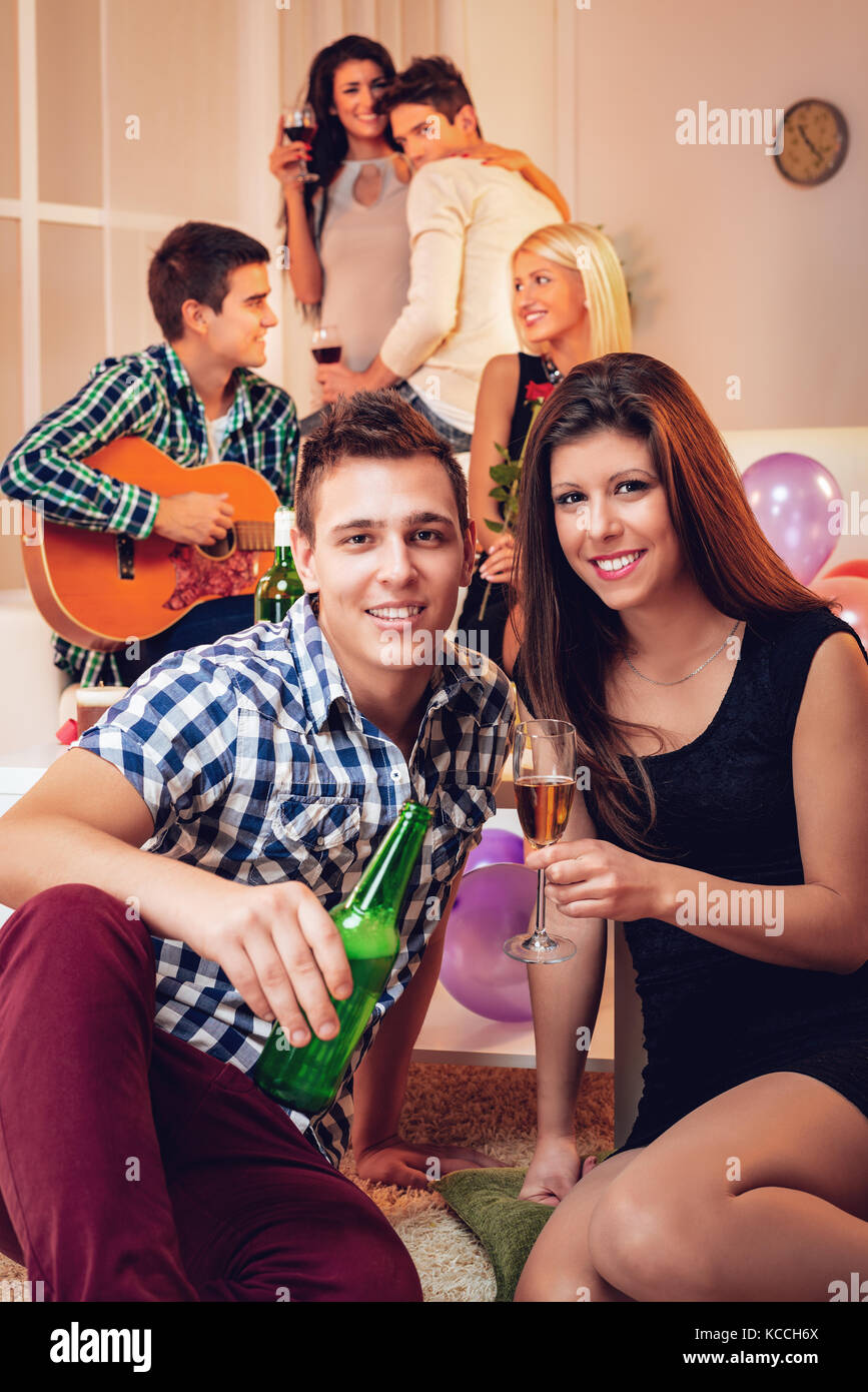 Young smiling couple at home party. They are sitting on the floor with ...
