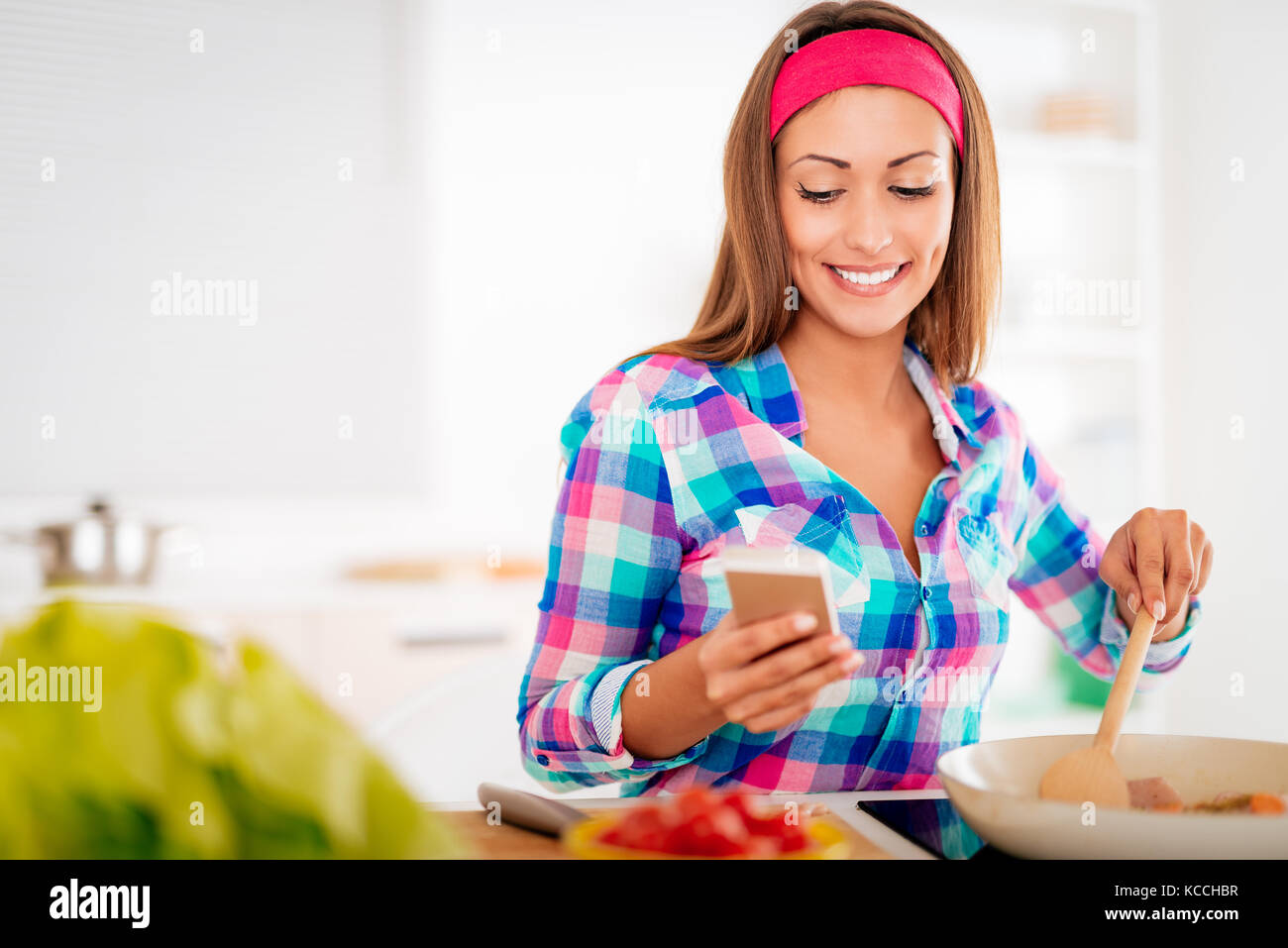 Cute happy girl making healthy meal and reading message at phone in the ...
