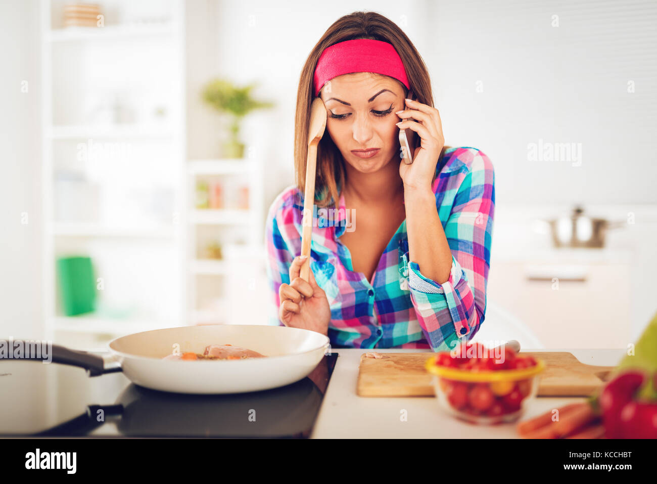 Beautiful young worried woman making meal and talking on the phone in ...