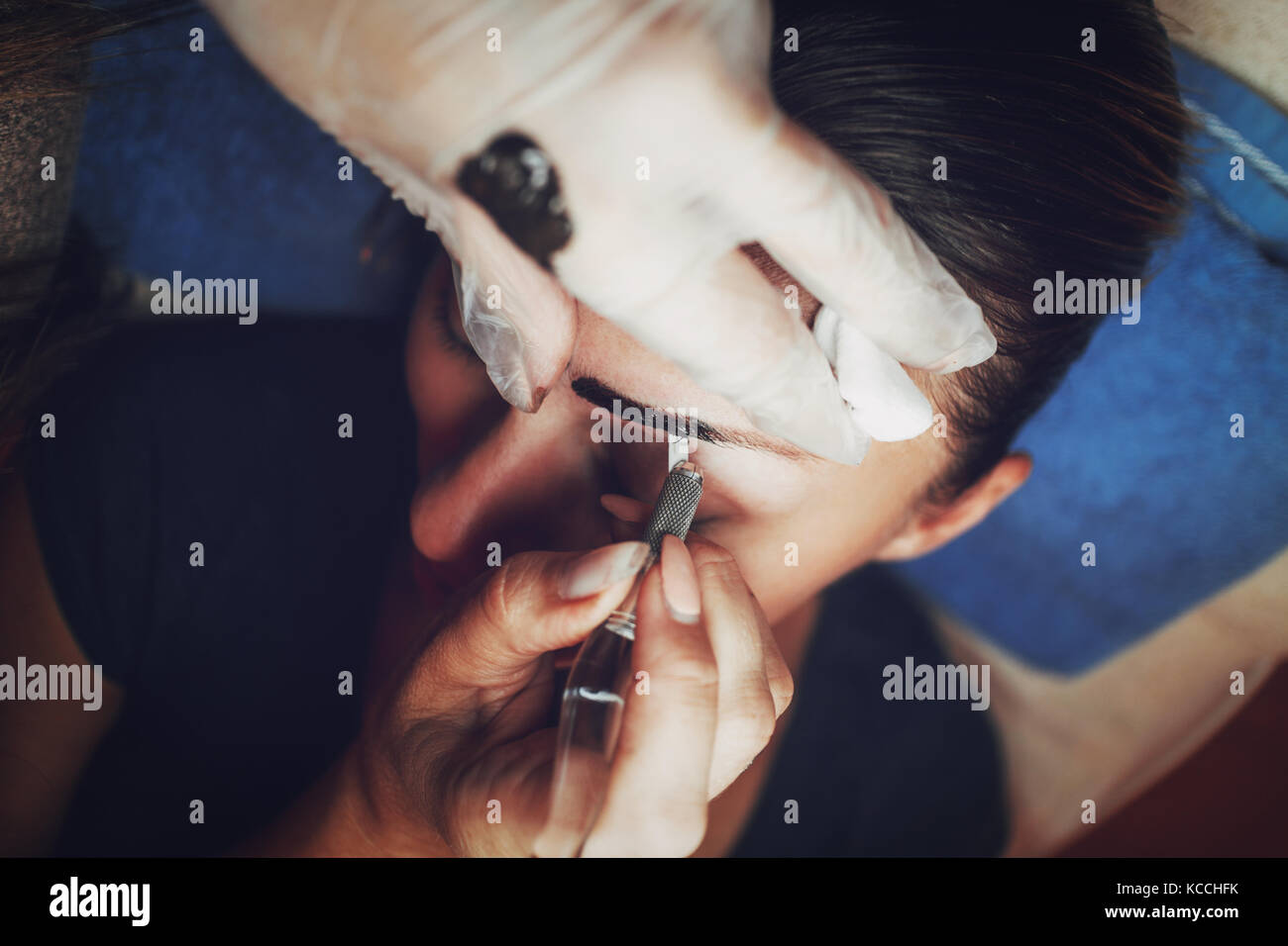 Closeup of a beautician hands microblading eyebrows to model with tool ...