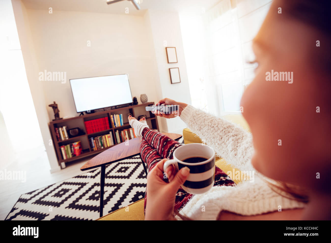 Rear view of a beautiful young woman watching a tv at living room ...