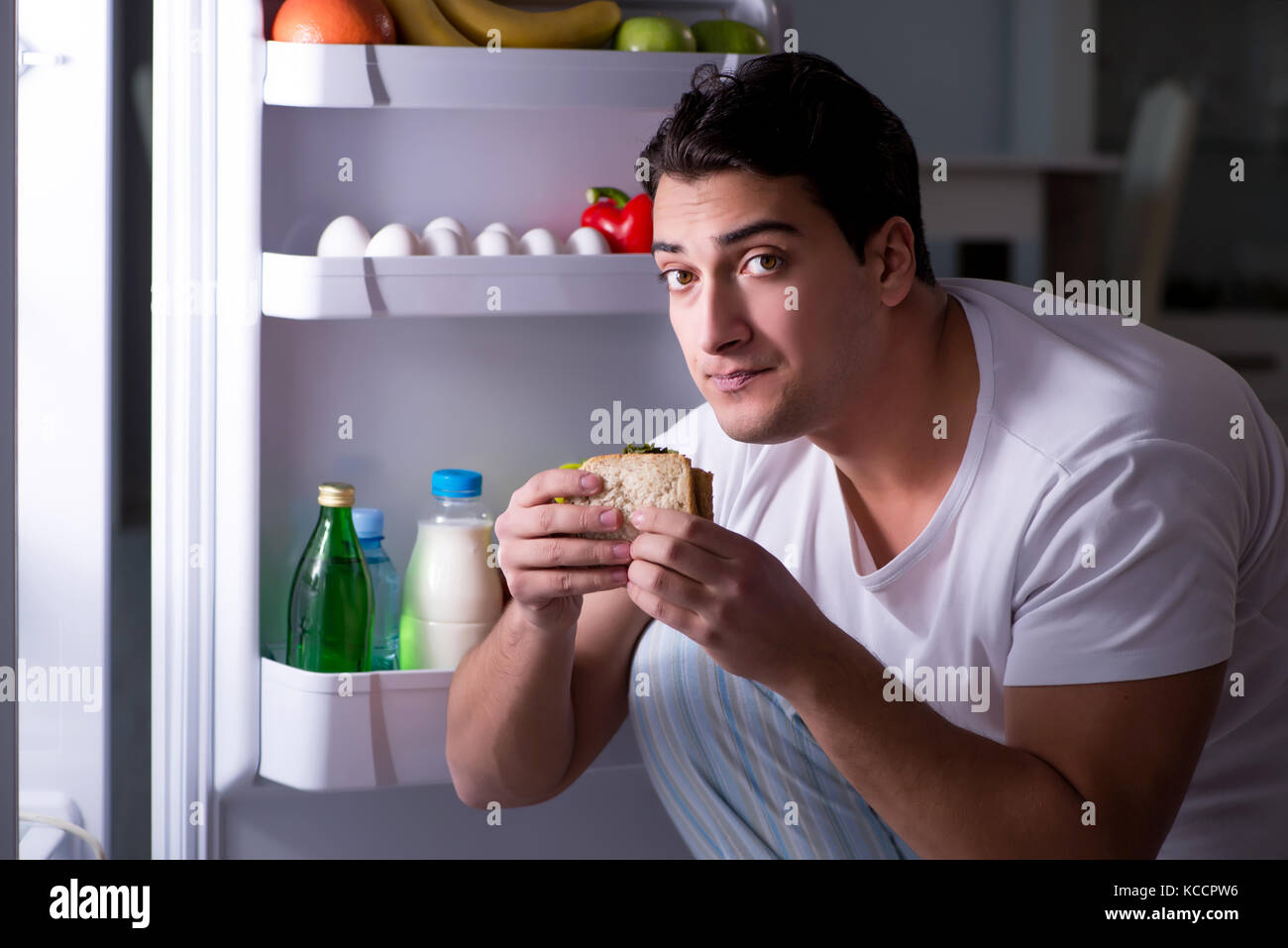 Man at the fridge eating at night Stock Photo - Alamy