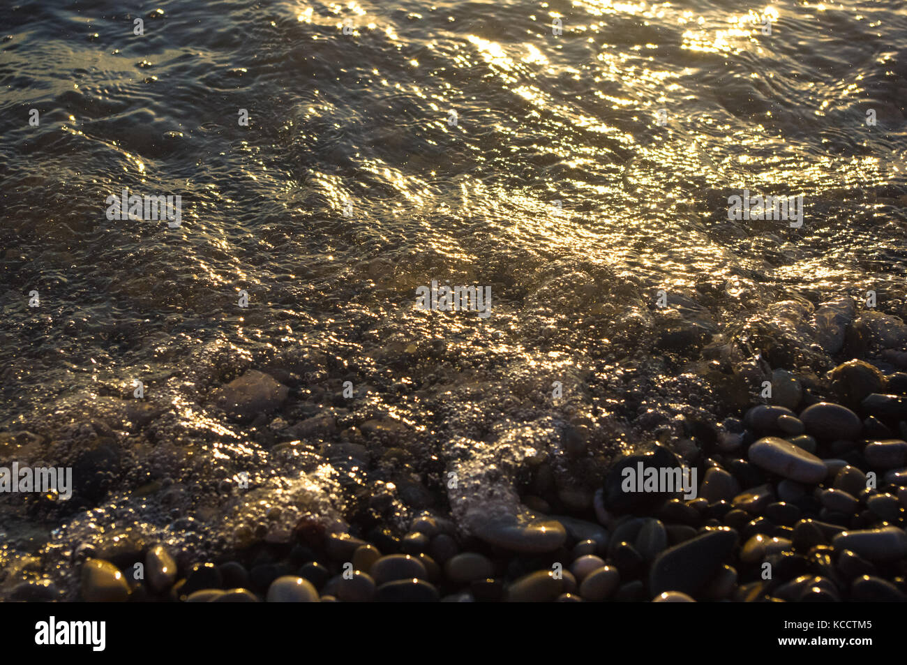 sea pebble beach with multicoloured stones, transparent waves with foam ...