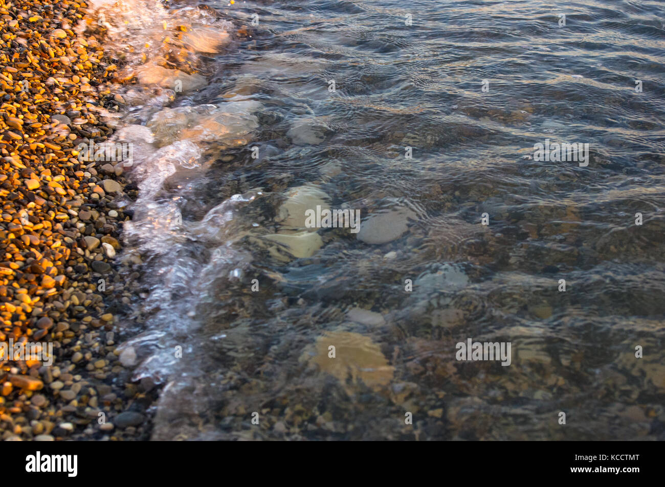 sea pebble beach with multicoloured stones, transparent waves with foam ...