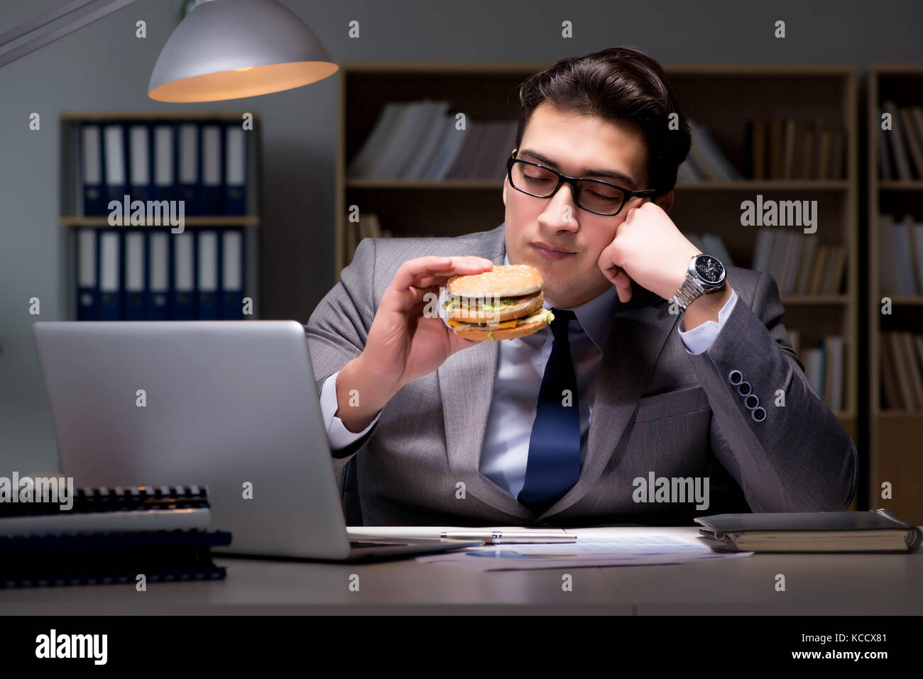 Businessman late at night eating a burger Stock Photo - Alamy