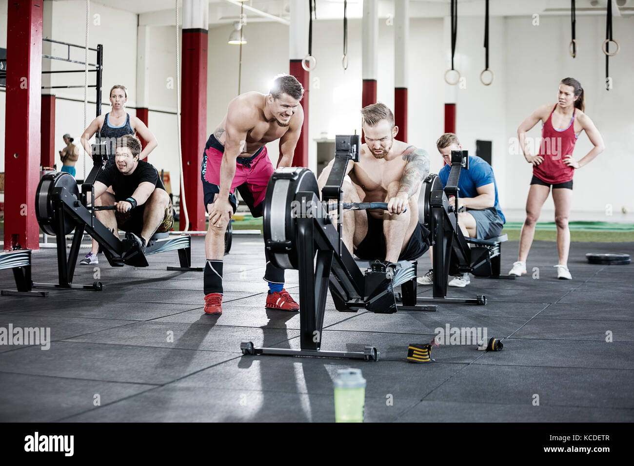 Tired clients looking at friends using rowing machines in gym Stock ...
