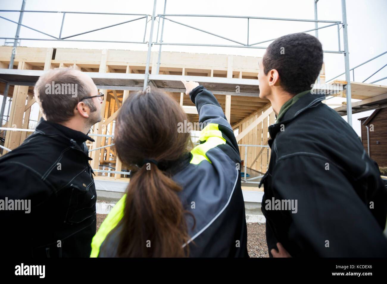 Rear view of female carpenter pointing towards incomplete building ...
