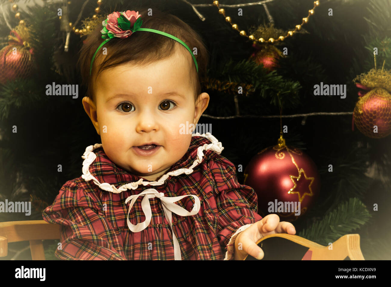 Little girl is sitting on wooden horse in front of Christmas tree ...