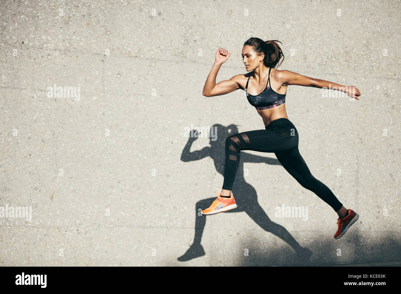 Young woman with fit body jumping and running against grey background ...