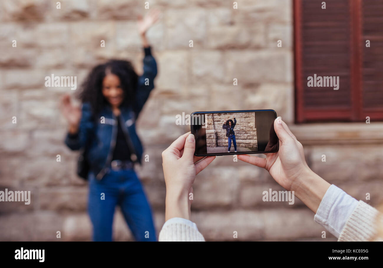 Woman clicking photo of her friend using mobile phone. Joyful woman ...