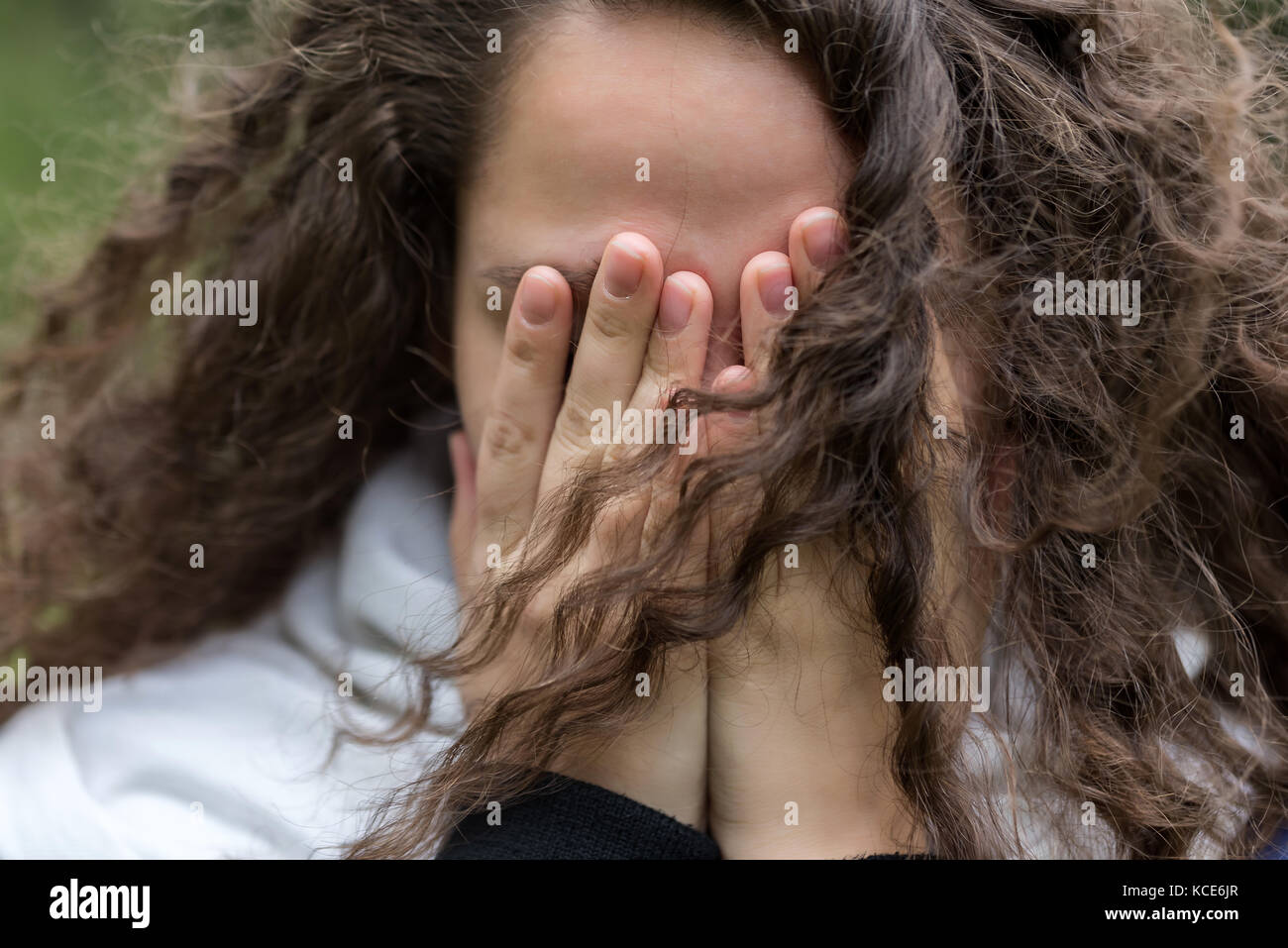 Portrait of a weeping girl with curly hair covering her face with her ...