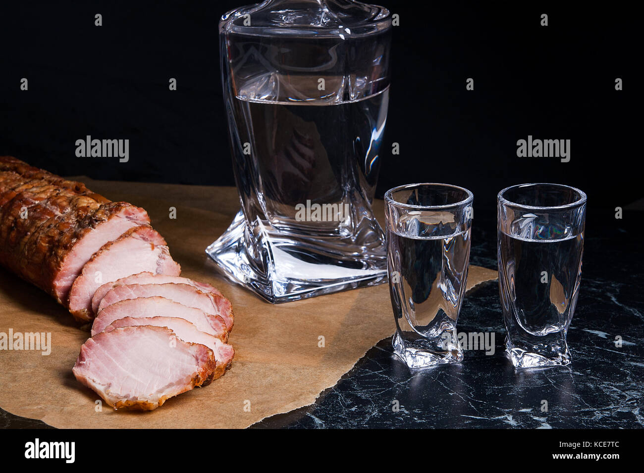 Bottle and shot glasses with vodka. Slices of smoked meat or ham on ...
