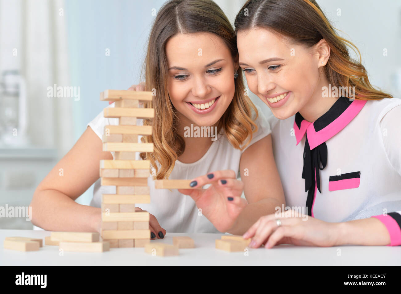 Two emotional sisters sitting at table and playing with wooden blocks ...