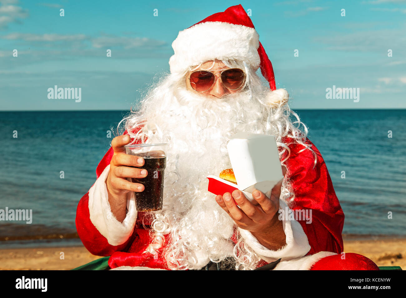 Santa Claus on the beach eating a hamburger. The concept of unhealthy ...