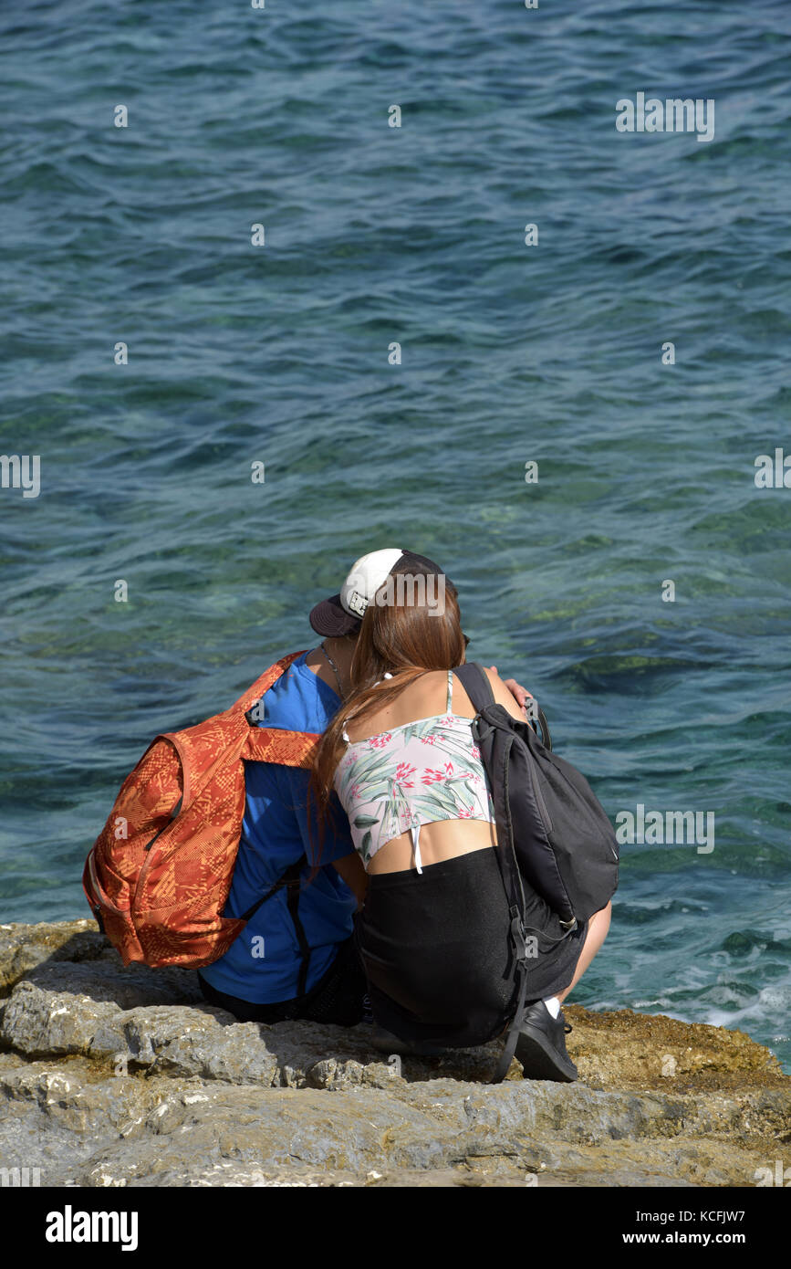 tow teenagers sitting on a beach or harbour wall next to the sea on ...