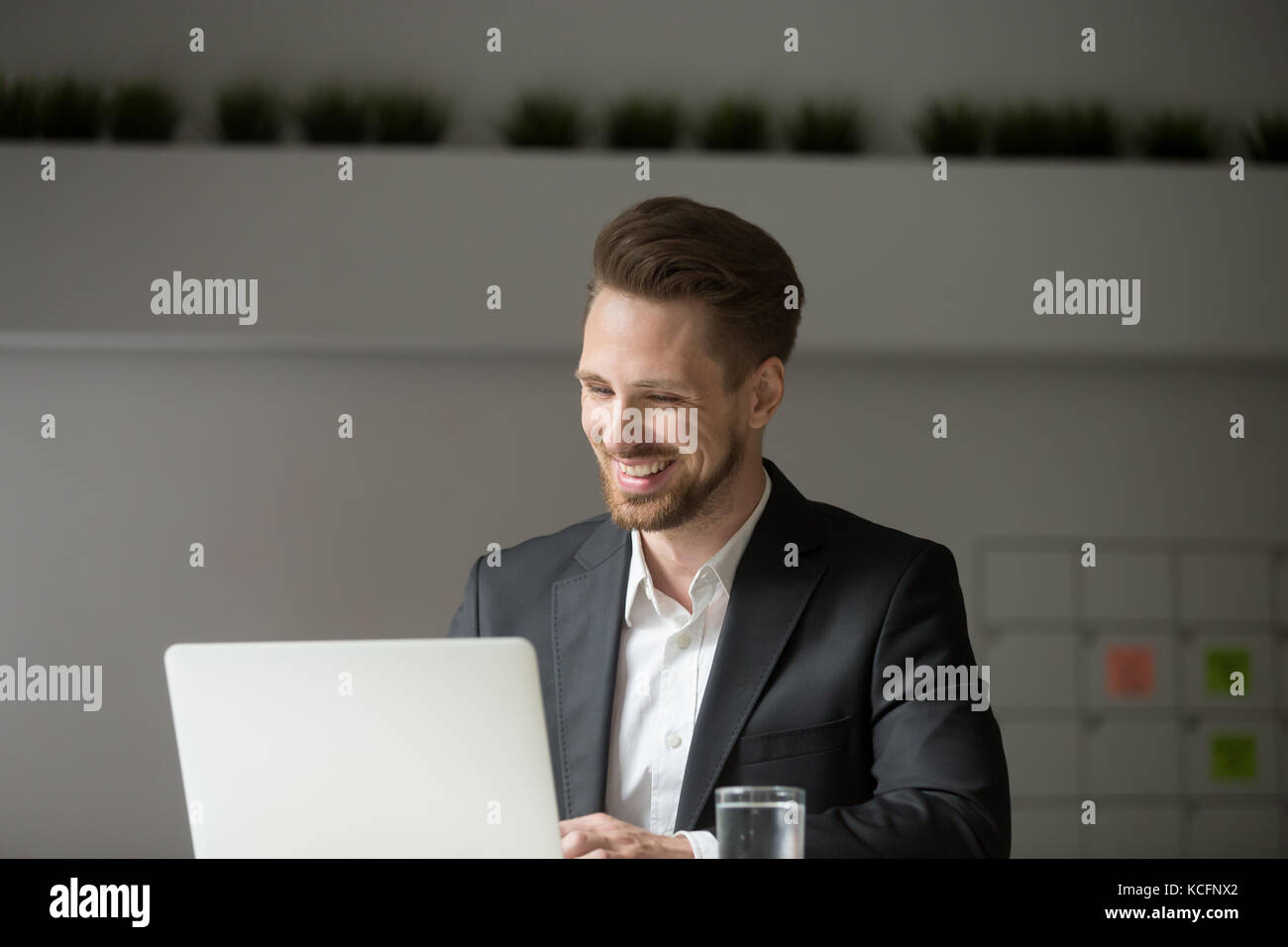 Handsome smiling businessman looking at laptop screen at work in office ...