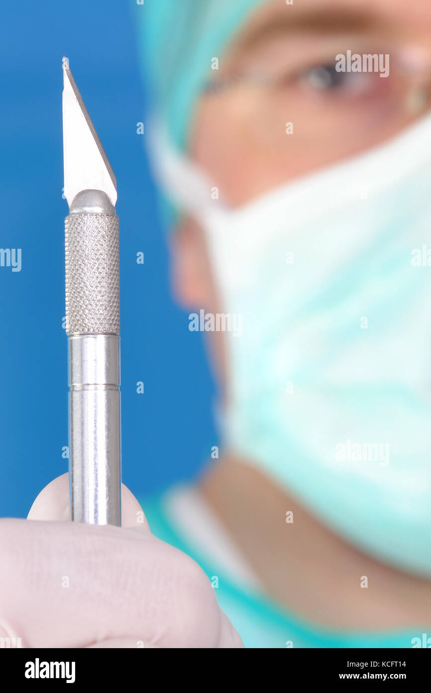 Closeup of surgeon holding scalpel up his face over blue background ...