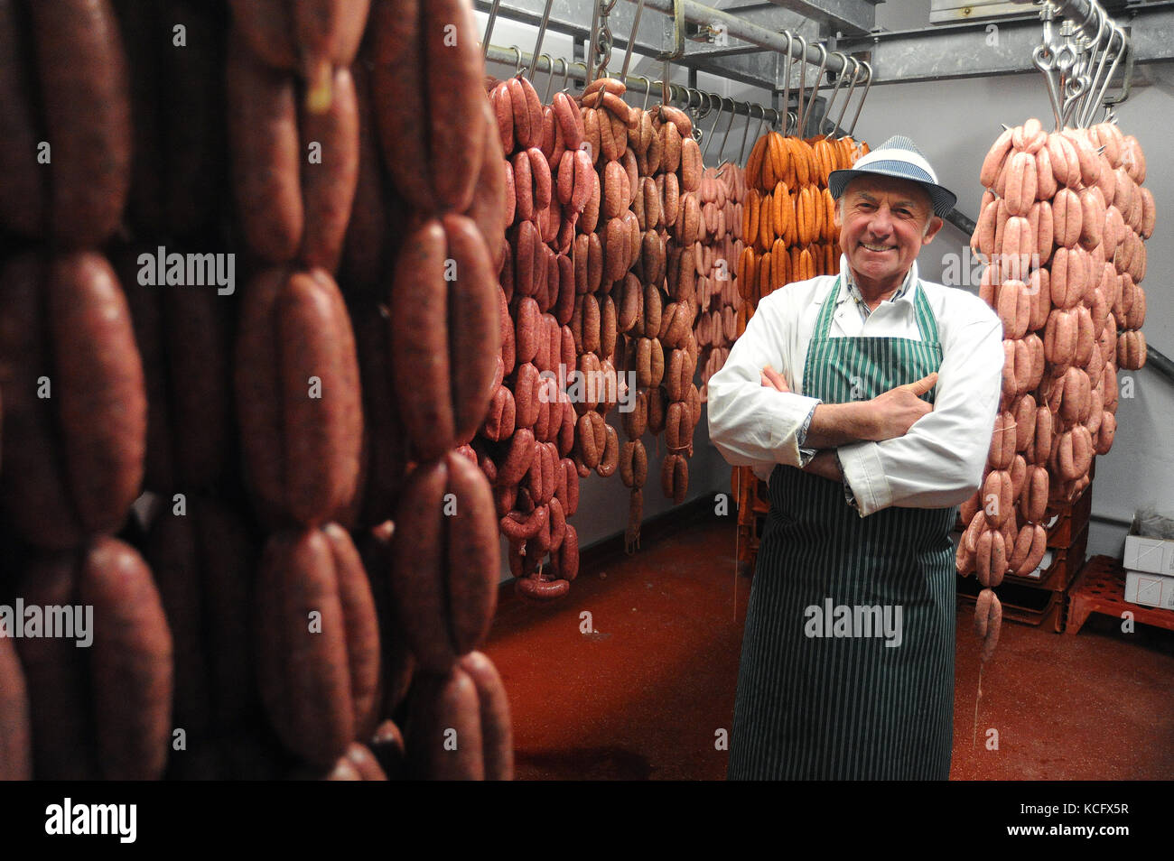 Portrait of a butcher in a walk in fridge filled with sausages in ...
