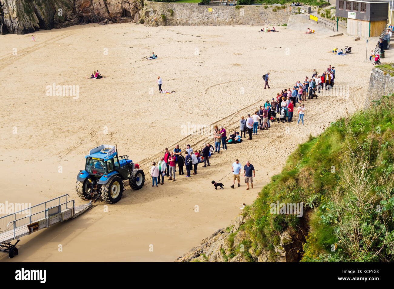 Long queue of people queueing by jetty tractor on Castle beach for boat ...