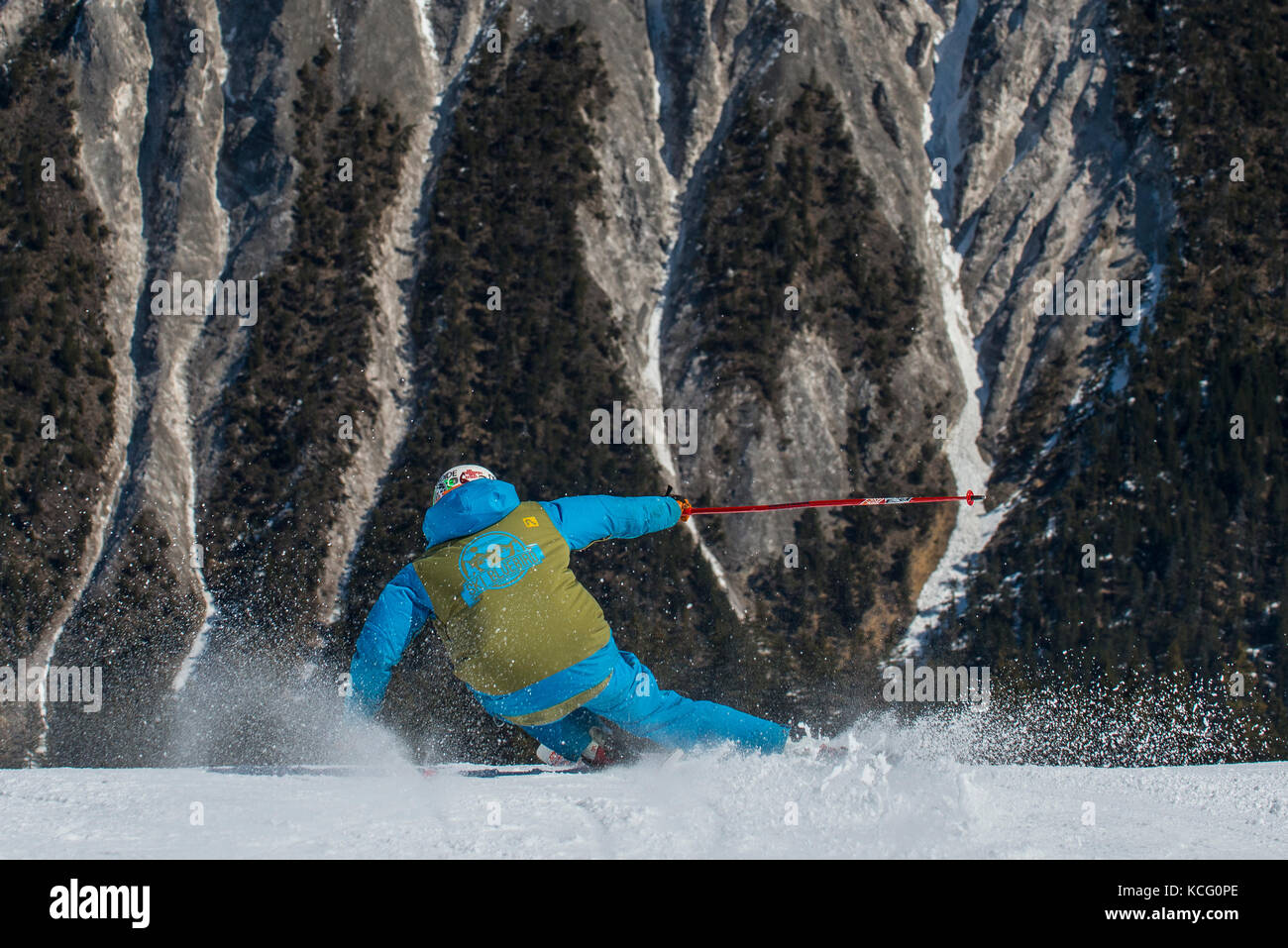 A skier carves a turn on piste with spines of rock in the background in ...