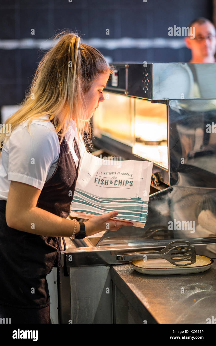 A young woman working servin fast food in a traditional british Fish ...