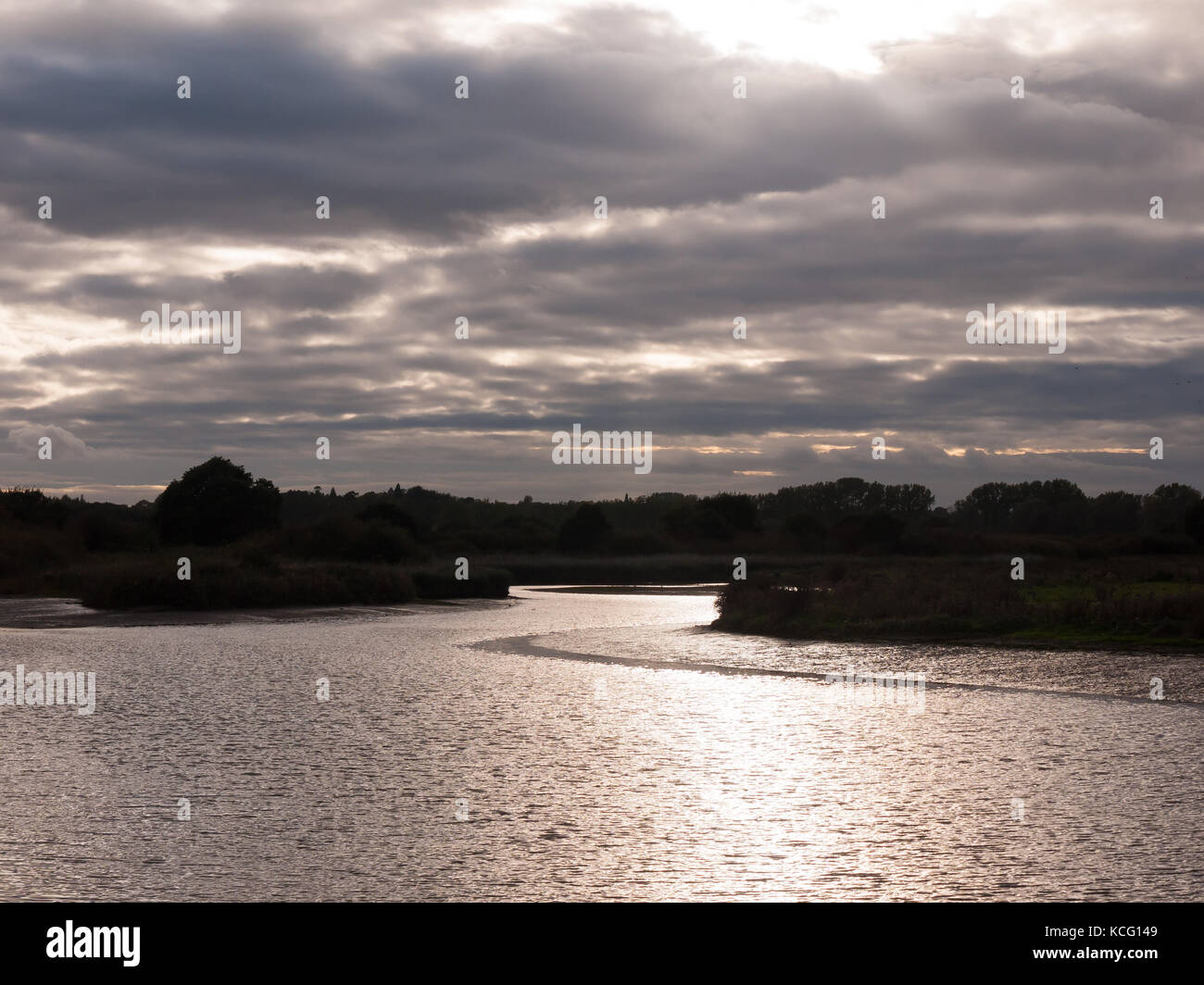sun setting through dramatic clouds and onto lake river stream water ...