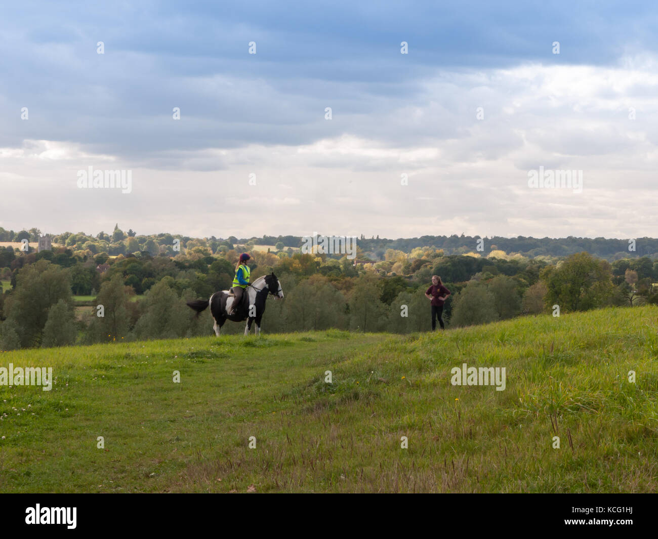 lady on horse in open field hill with dramatic sky and young person ...