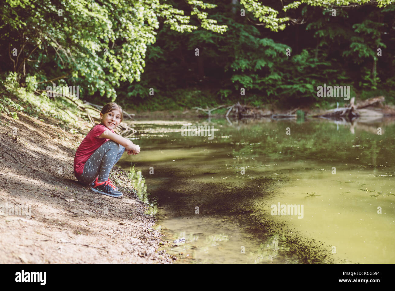 Girl squatting by the lake and smiling Stock Photo - Alamy