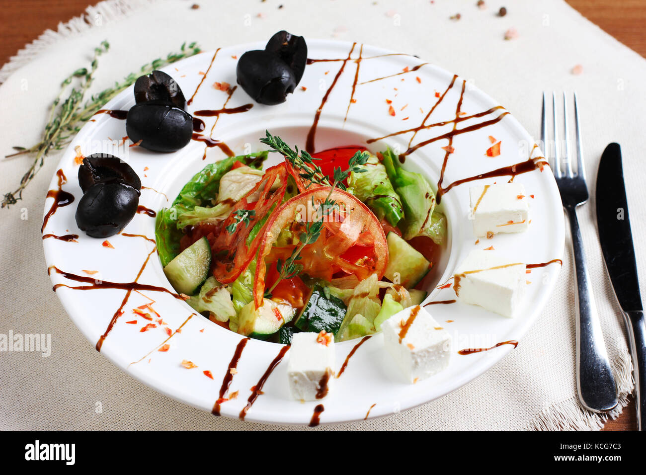 Greek salad in the white deep plate with the fork and knife Stock Photo ...