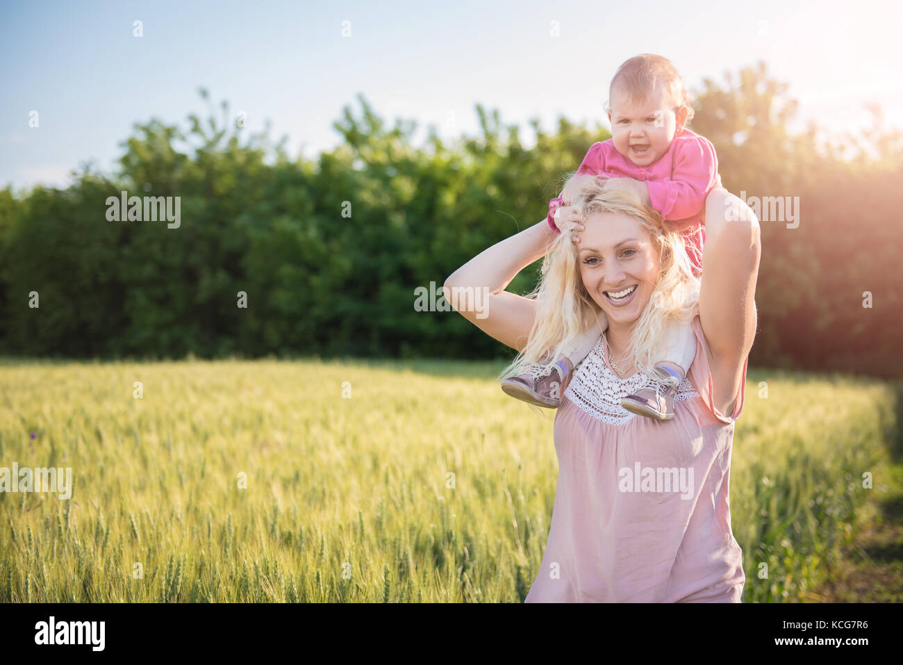 Mother Carrying Baby Daughter Piggyback and standing by the wheat field ...