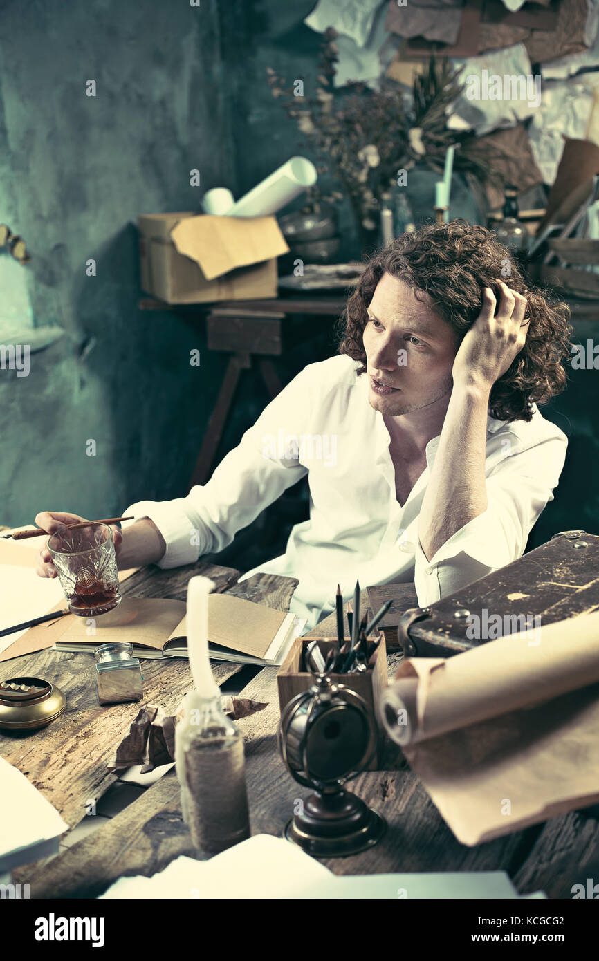 Writer at work. Handsome young writer sitting at the table and writing ...