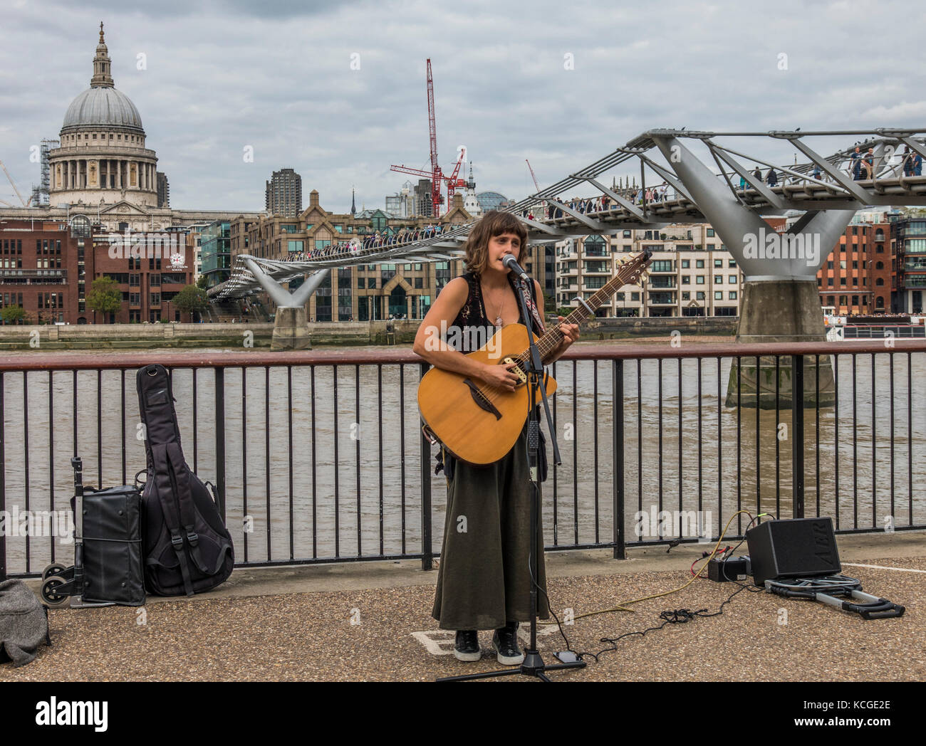 A young woman busker, singing and playing acoustic guitar, with ...