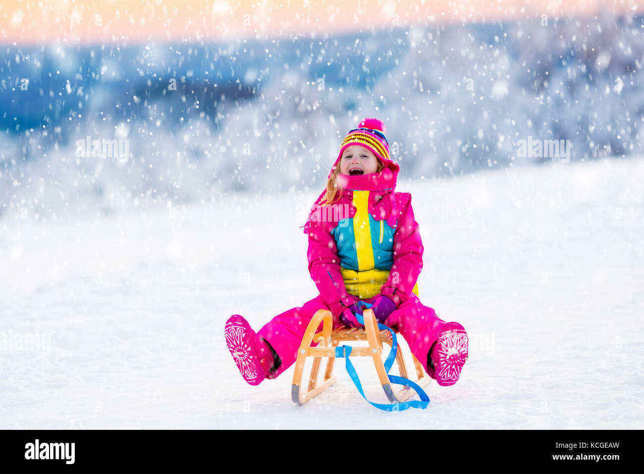Little girl enjoying a sleigh ride. Child sledding. Toddler kid riding a sledge. Children play ...